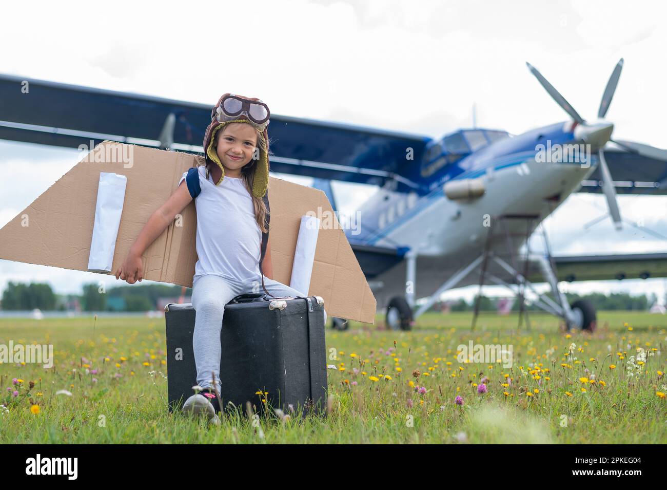 A little girl plays a pilot on the background of a small plane with a ...