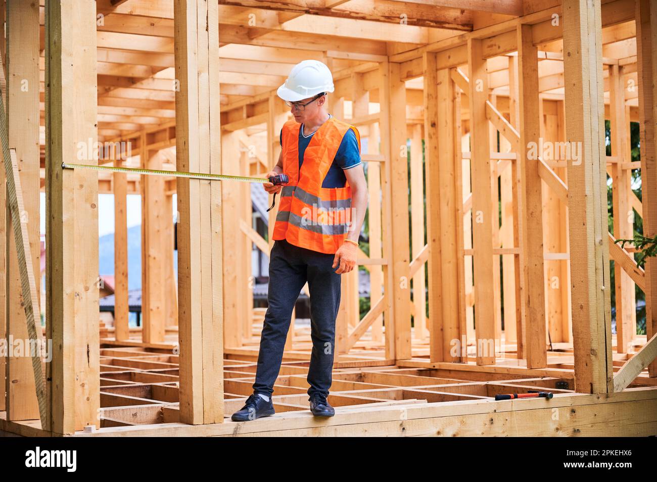 Carpenter constructing wooden skeleton building. Man measures distances ...