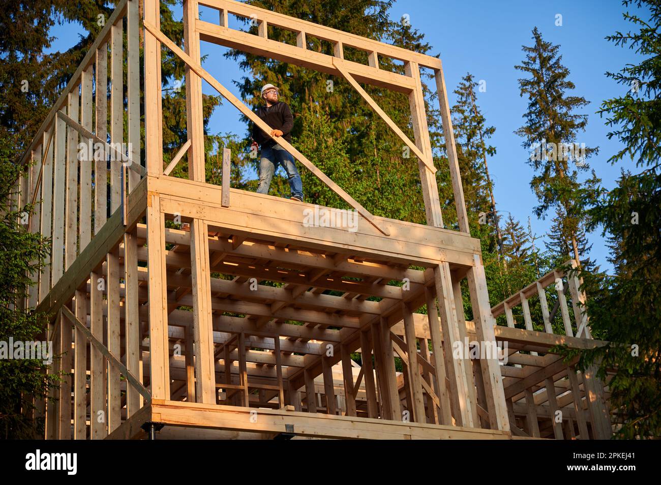 Carpenter constructing wooden framed two-story house near the forest ...