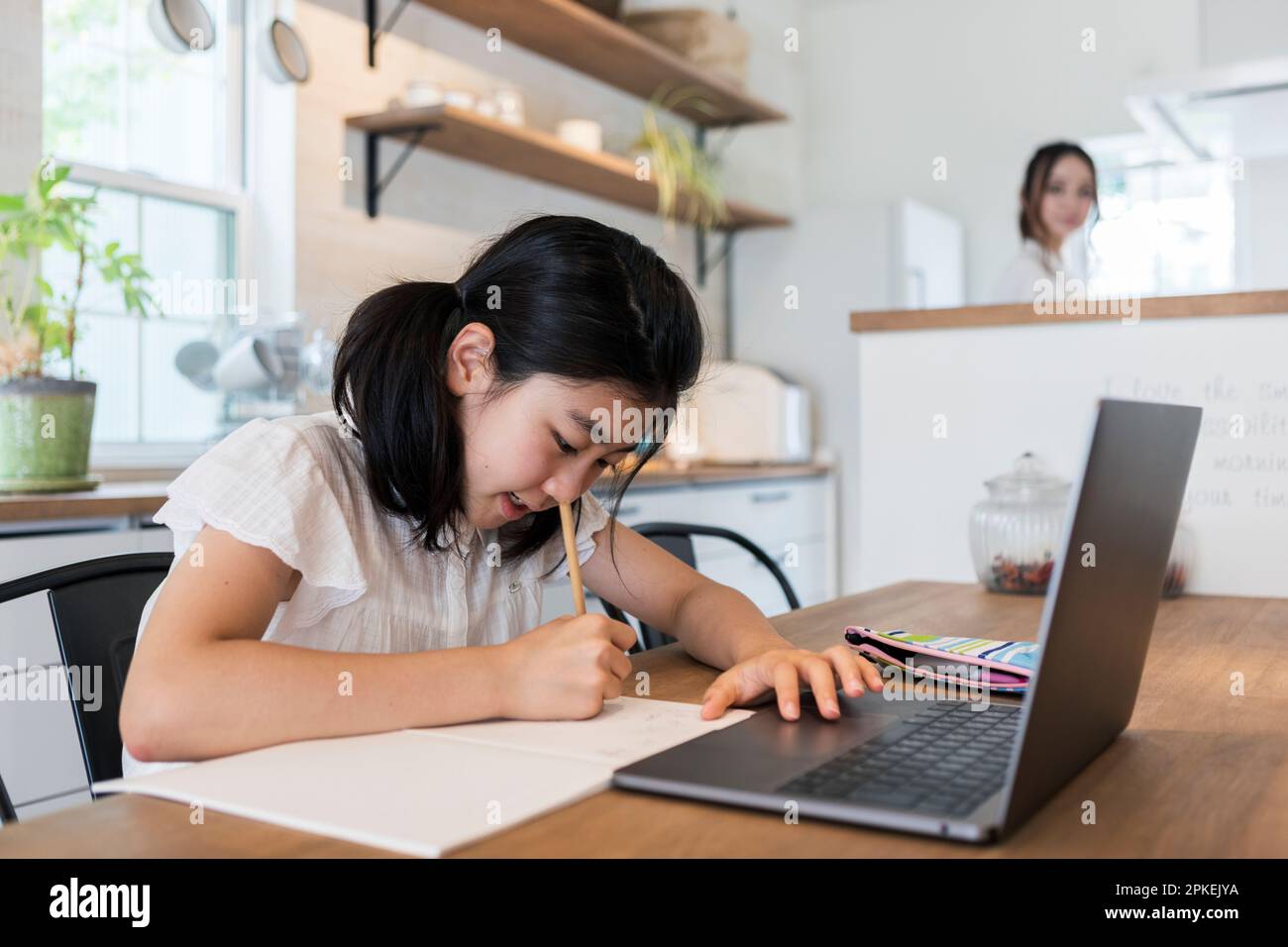Mother doing housework with girl taking online class Stock Photo - Alamy