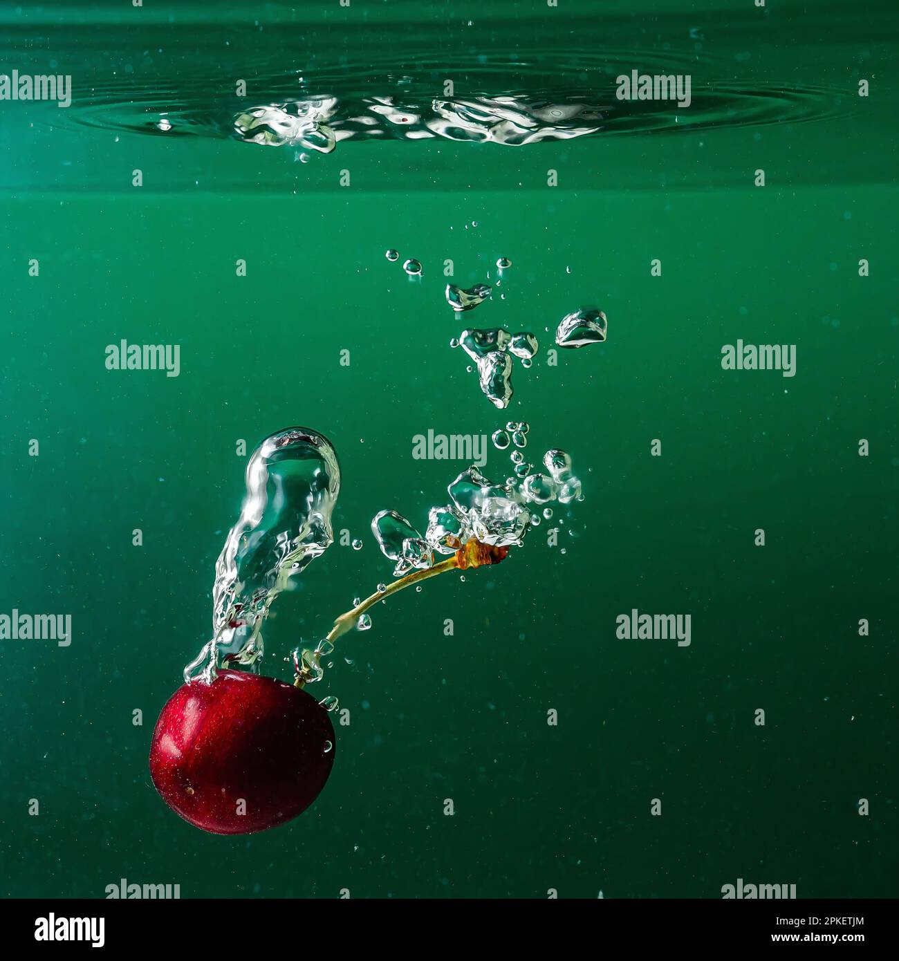 ripe cherries fall into the water raising splashes and air bubbles ...