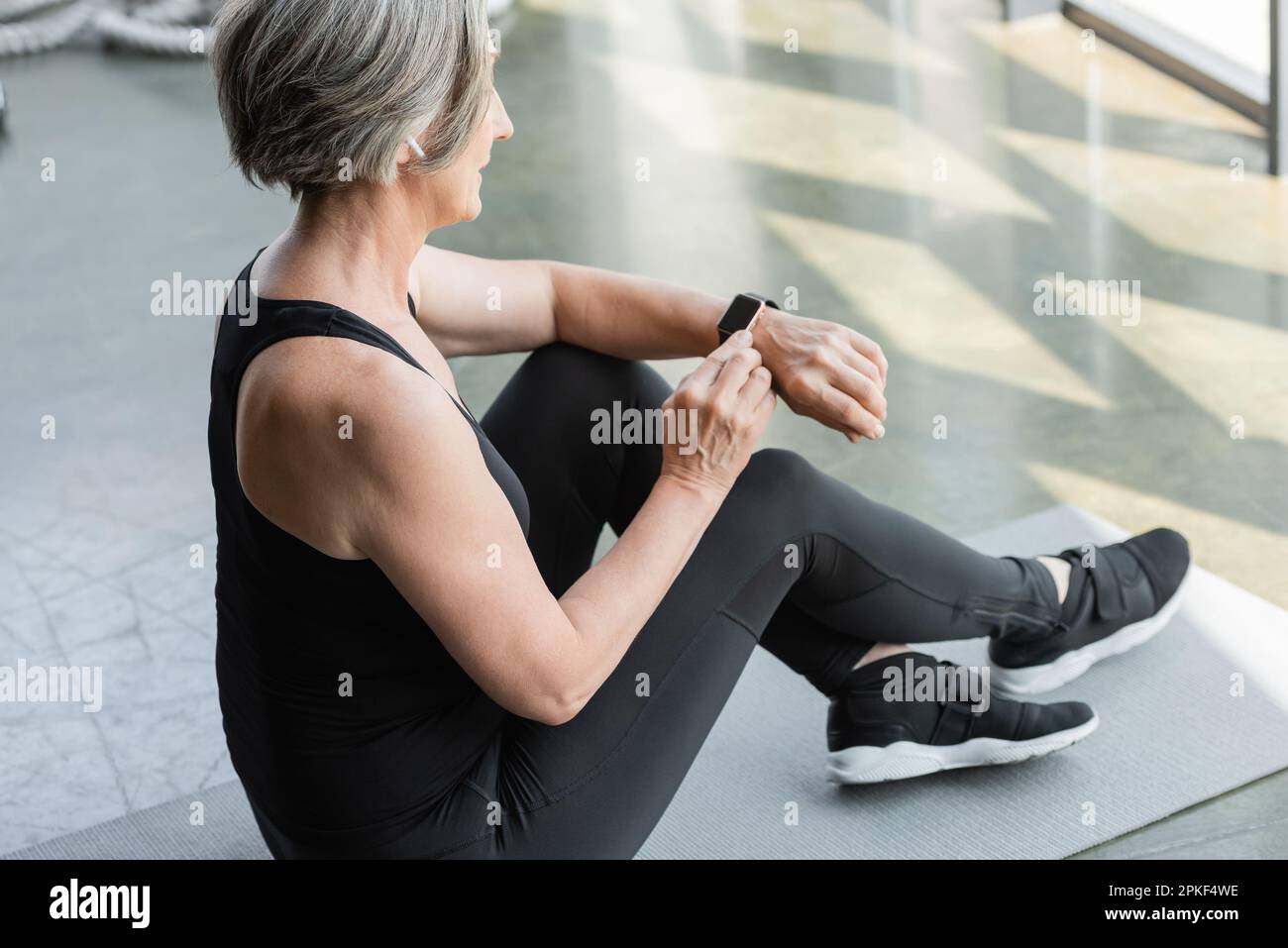 fit senior woman with grey hair sitting and using fitness tracker after ...