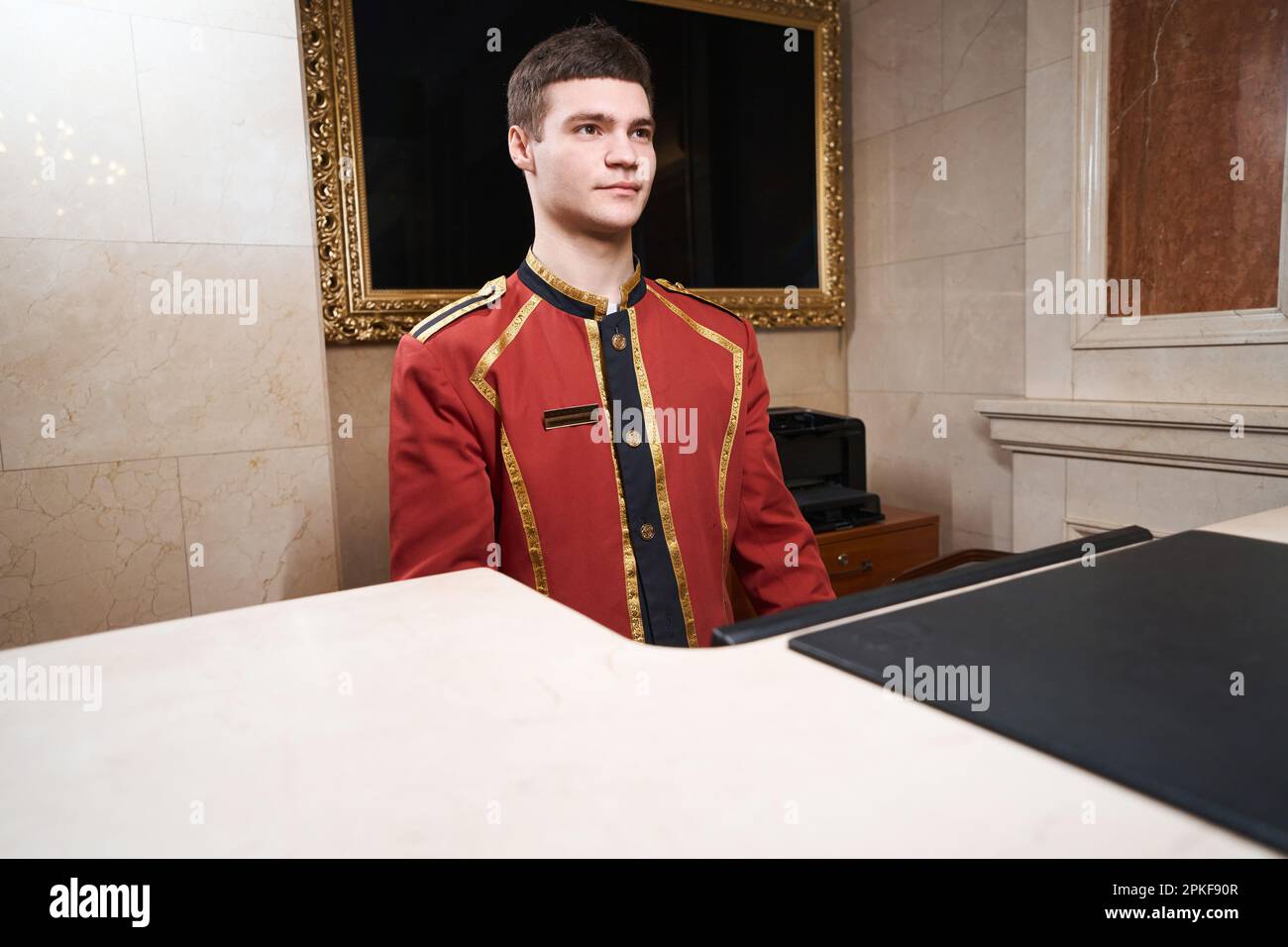 Young pleasant bellhop is standing at the reception desk Stock Photo ...