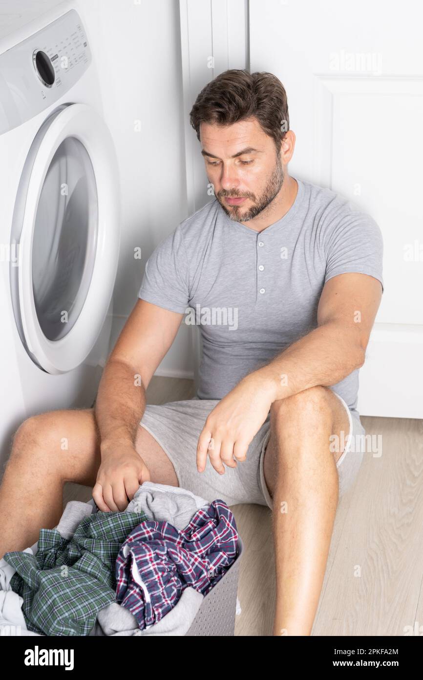Man with clothes near washing machine. Handsome man sits in front of ...