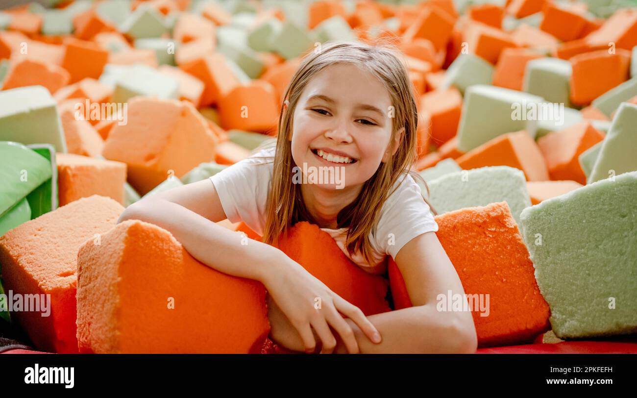 Pretty child girl in trampoline park having fun in colorful soft cubes ...