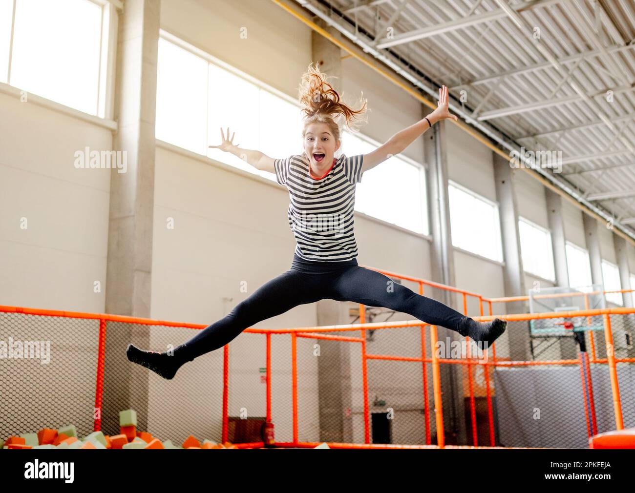 Pretty girl in trampoline park jumping with split and smiling. Happy ...