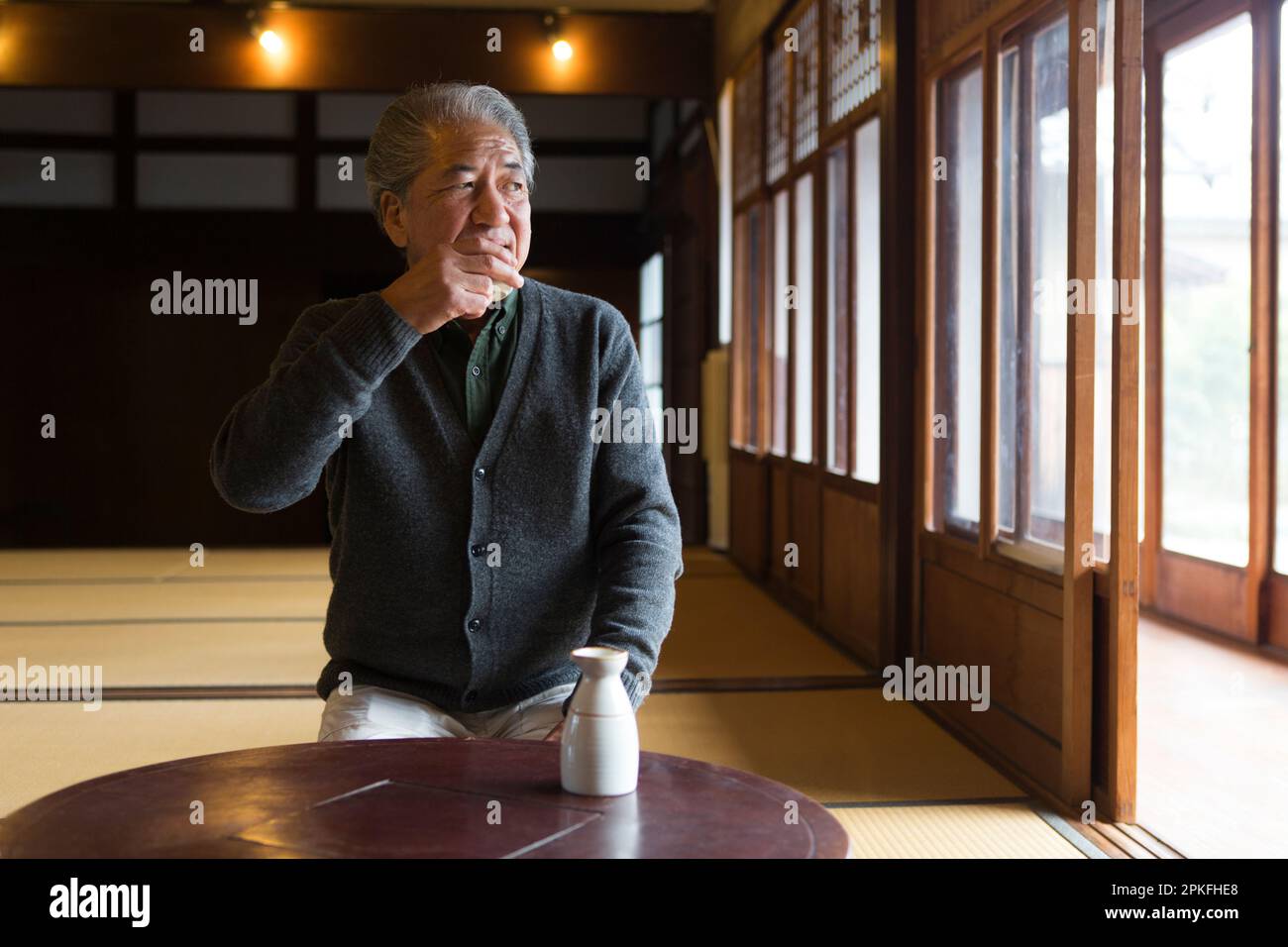 Senior man drinking sake at an old private house where he is traveling ...