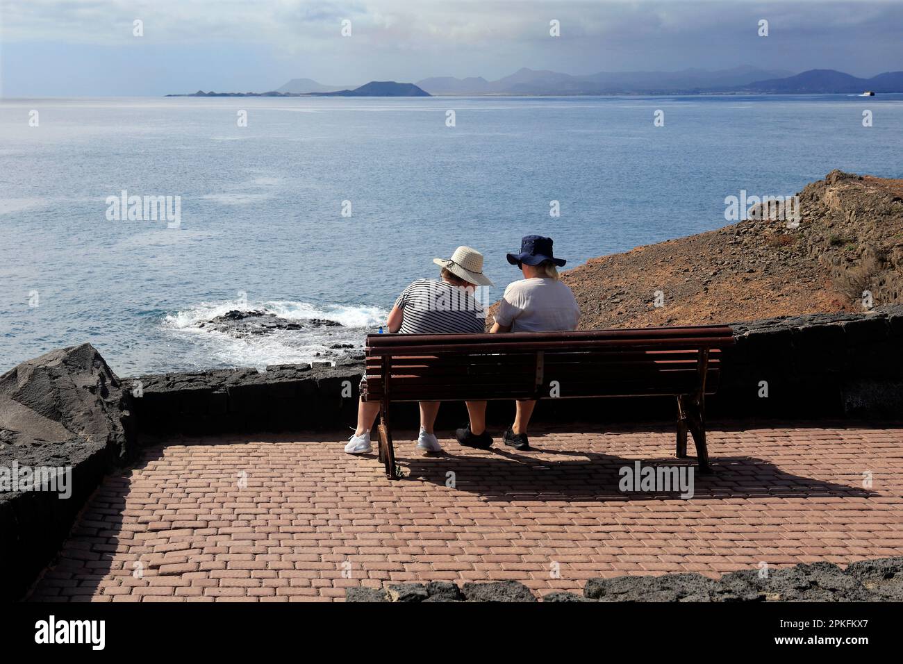 Two mature women wearing hats sitting companionably on a bench, looking ...
