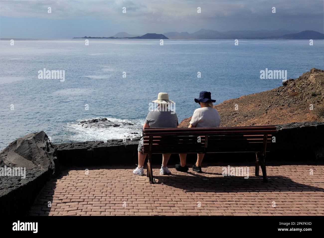 Two mature women wearing hats sitting companionably on a bench, looking ...