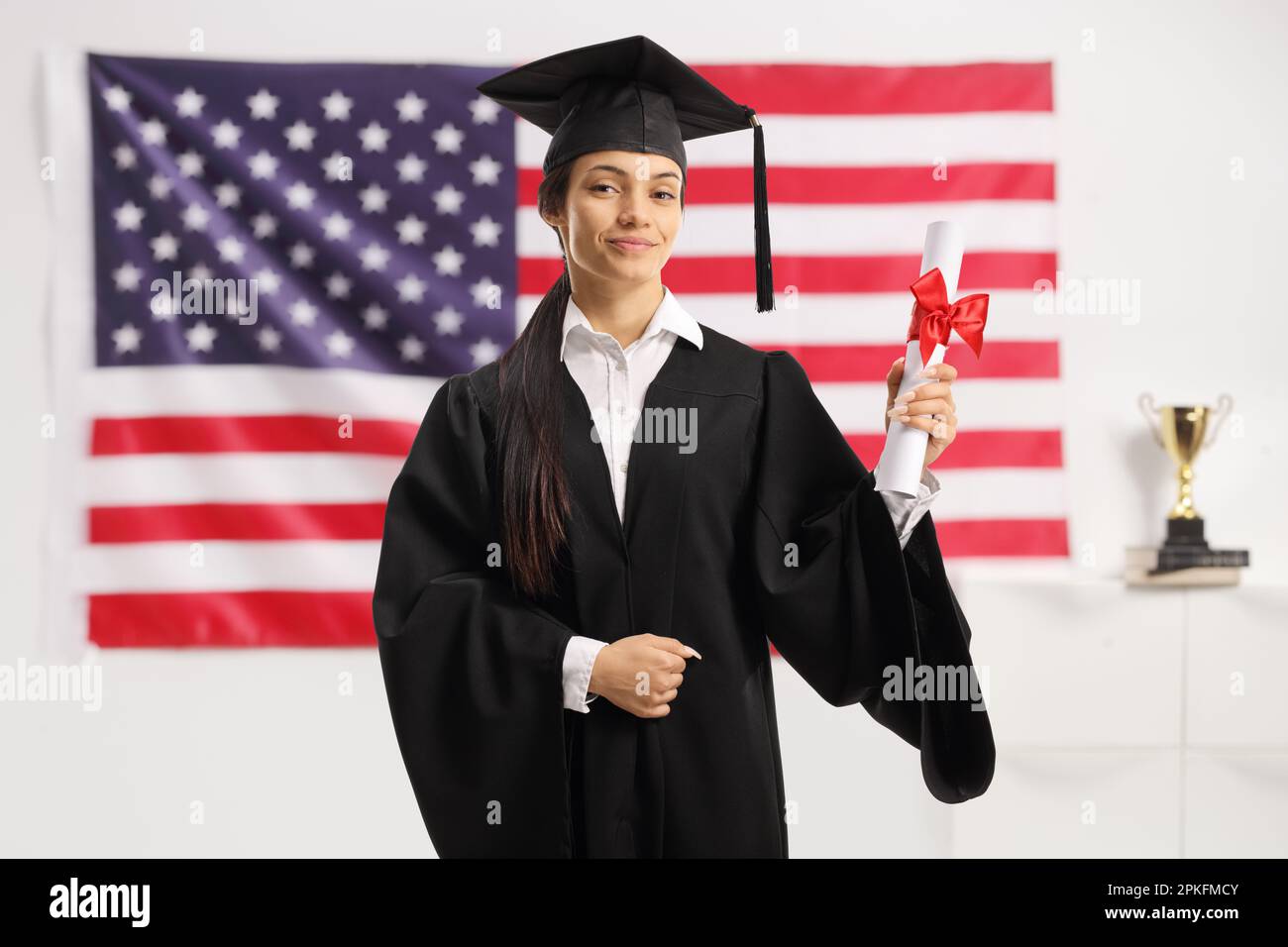 Young woman in a graduation gown holding a diploma in front of USA flag ...