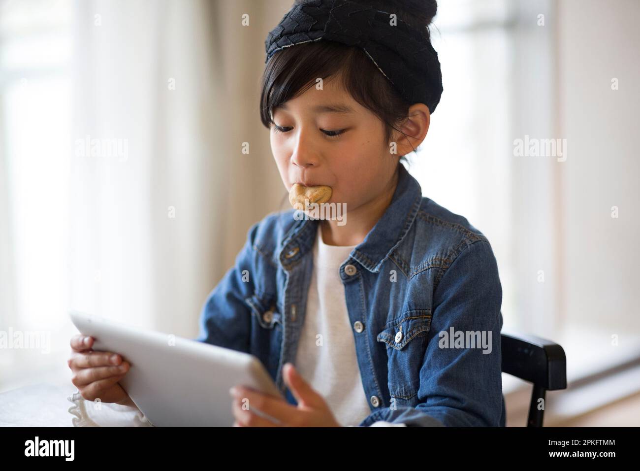 An elementary school girl operating a tablet while eating a snack Stock ...