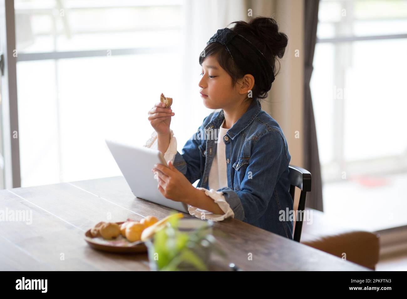 An elementary school girl operating a tablet while eating a snack Stock ...