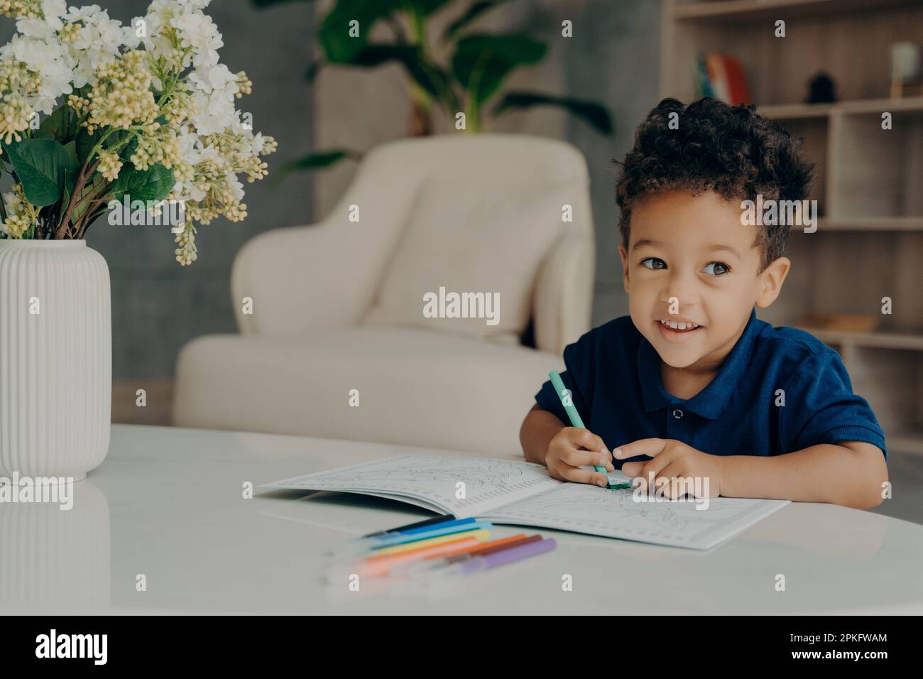 Happy curly mixed race boy coloring animals in coloring book with felt ...