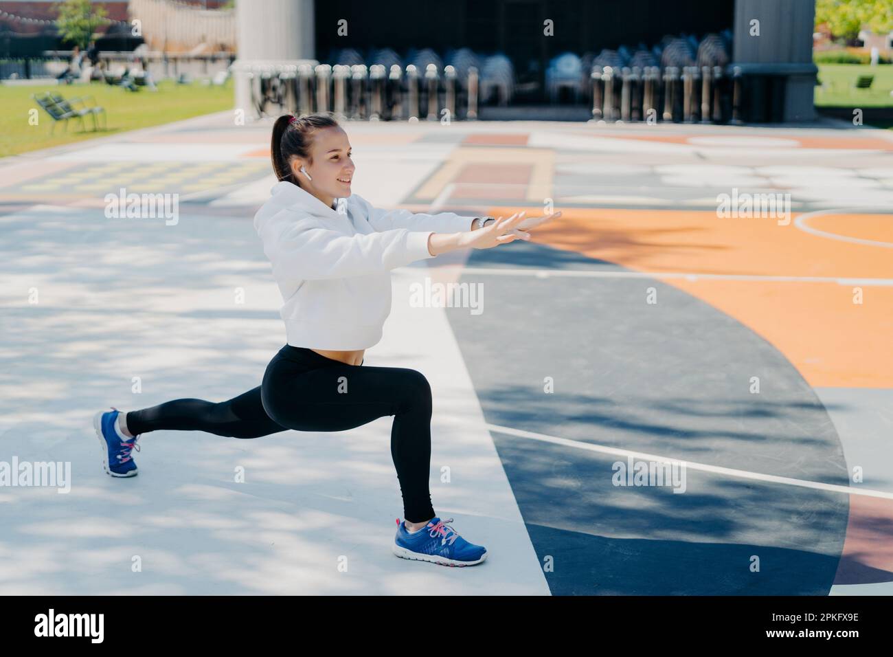 Horizontal shot of motivated sporty woman stretches legs and arms does ...