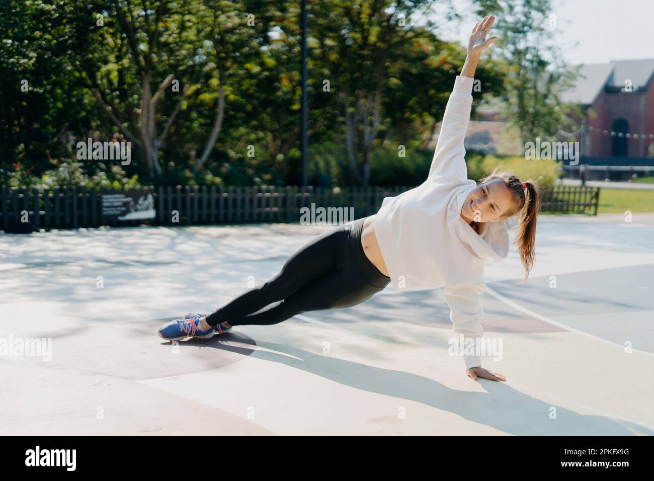 Glad energetic dark haired woman stands in sideways plank keeps arm ...