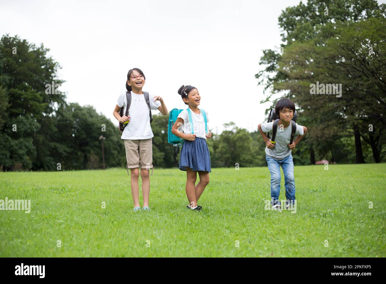 Elementary school children standing on a grassy field in a park with ...