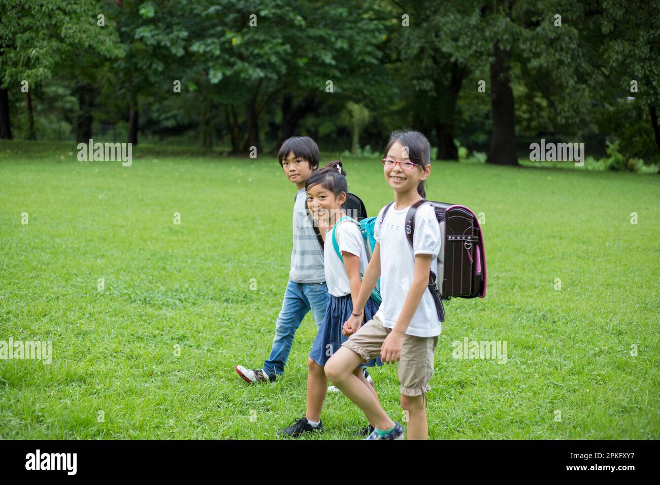 Elementary school children with school backpacks walking hand in hand in a meadow Stock Photo ...