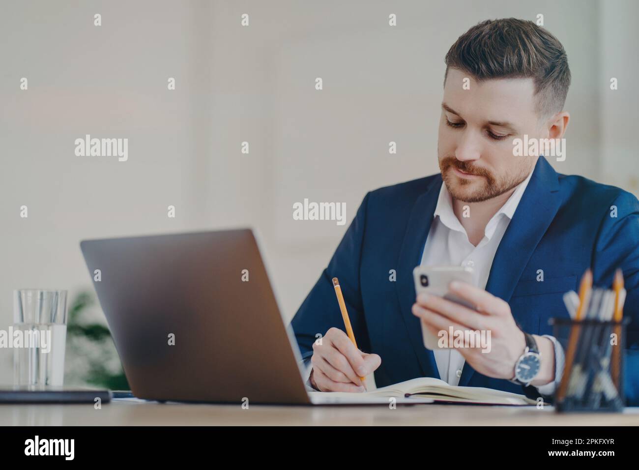 Young successful businessman with mobile phone in hand writing down ...