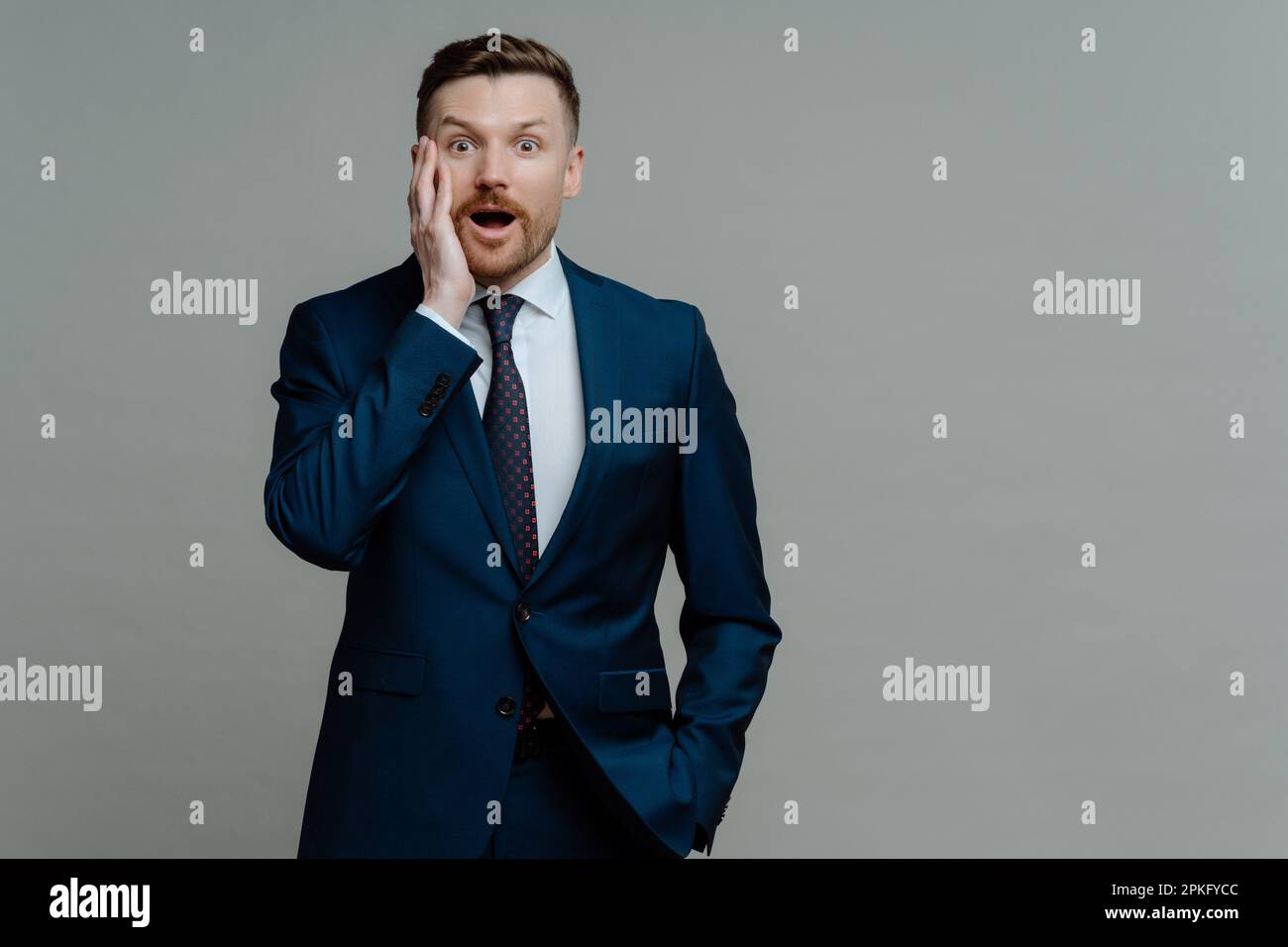 Unbelievable news. Young shocked businessman in suit looking at camera ...