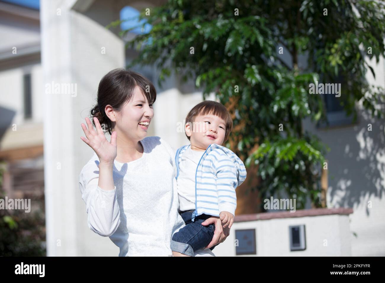 Wife holding a baby waving her hand to send him off Stock Photo - Alamy