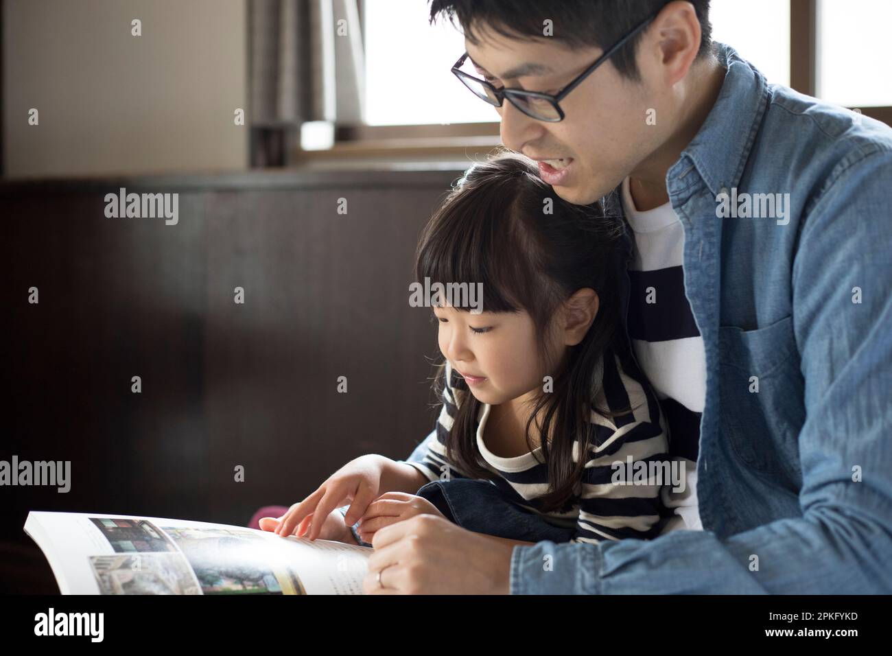 Girl sitting on father's lap and having book read to her Stock Photo ...
