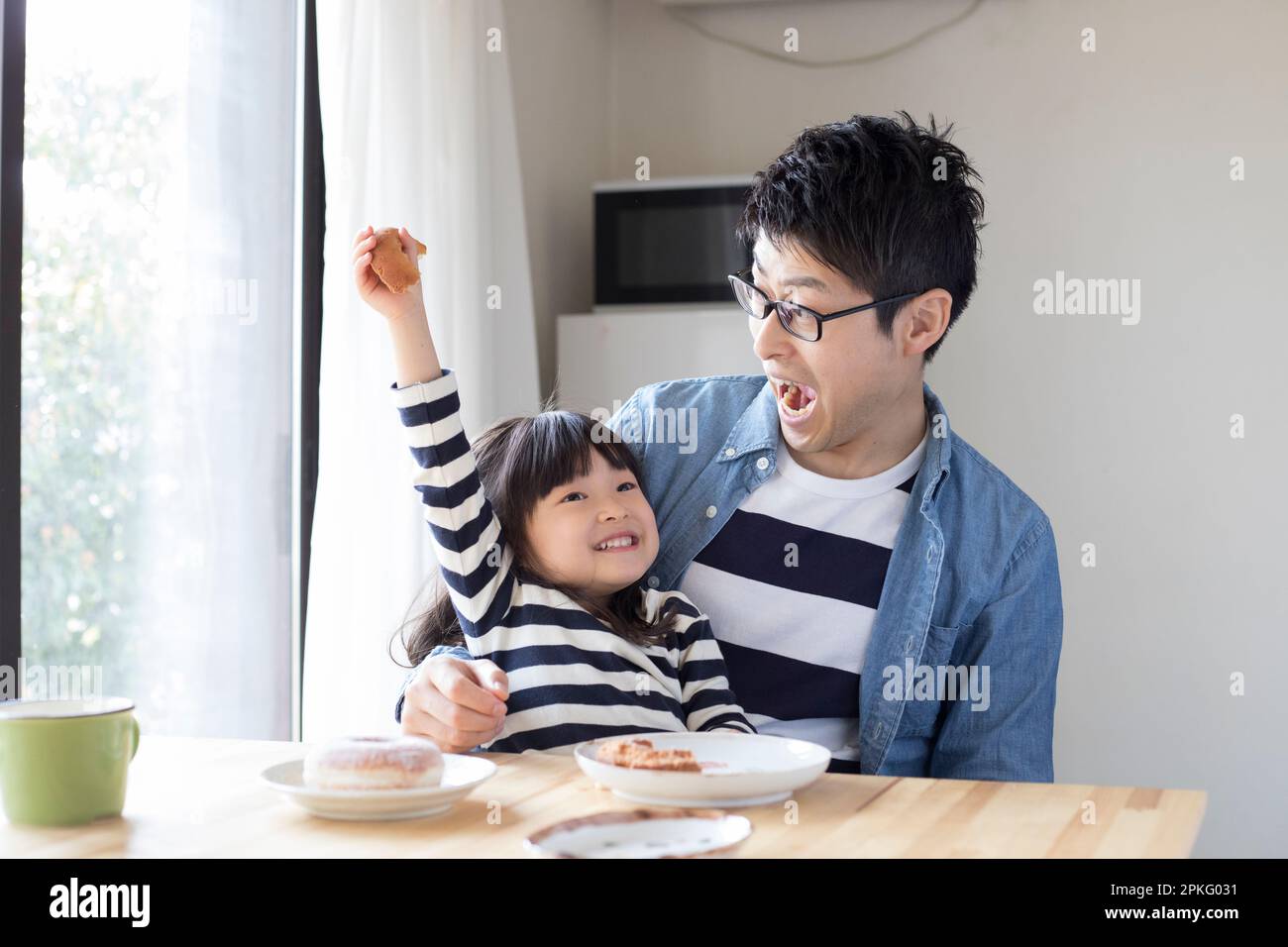 Girl sitting on father's lap and trying to eat donut as a snack Stock ...