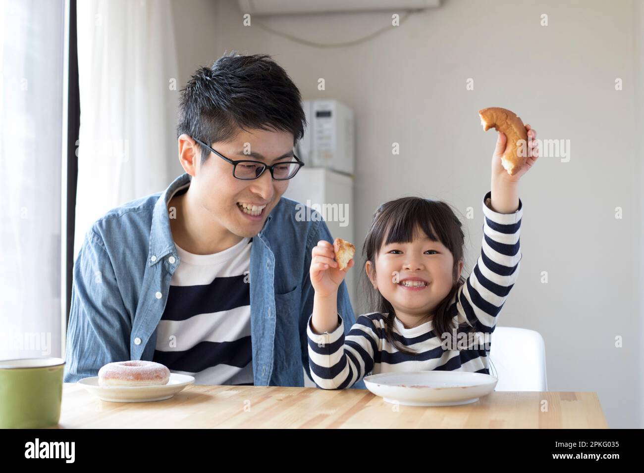 Girl trying to eat donut and father watching her Stock Photo - Alamy