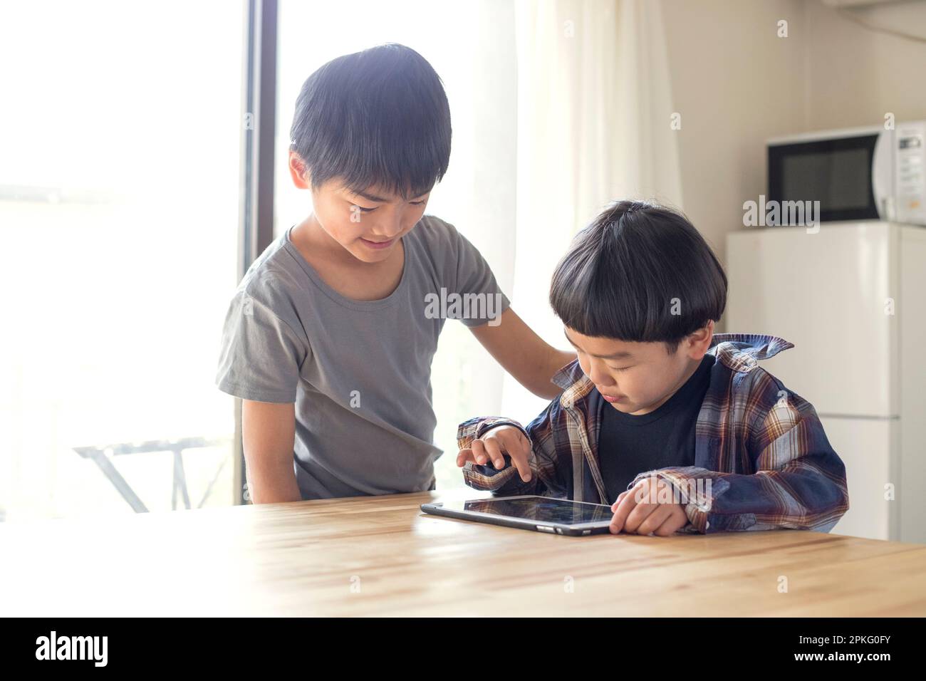 A little brother learning how to use the tablet from his older brother ...