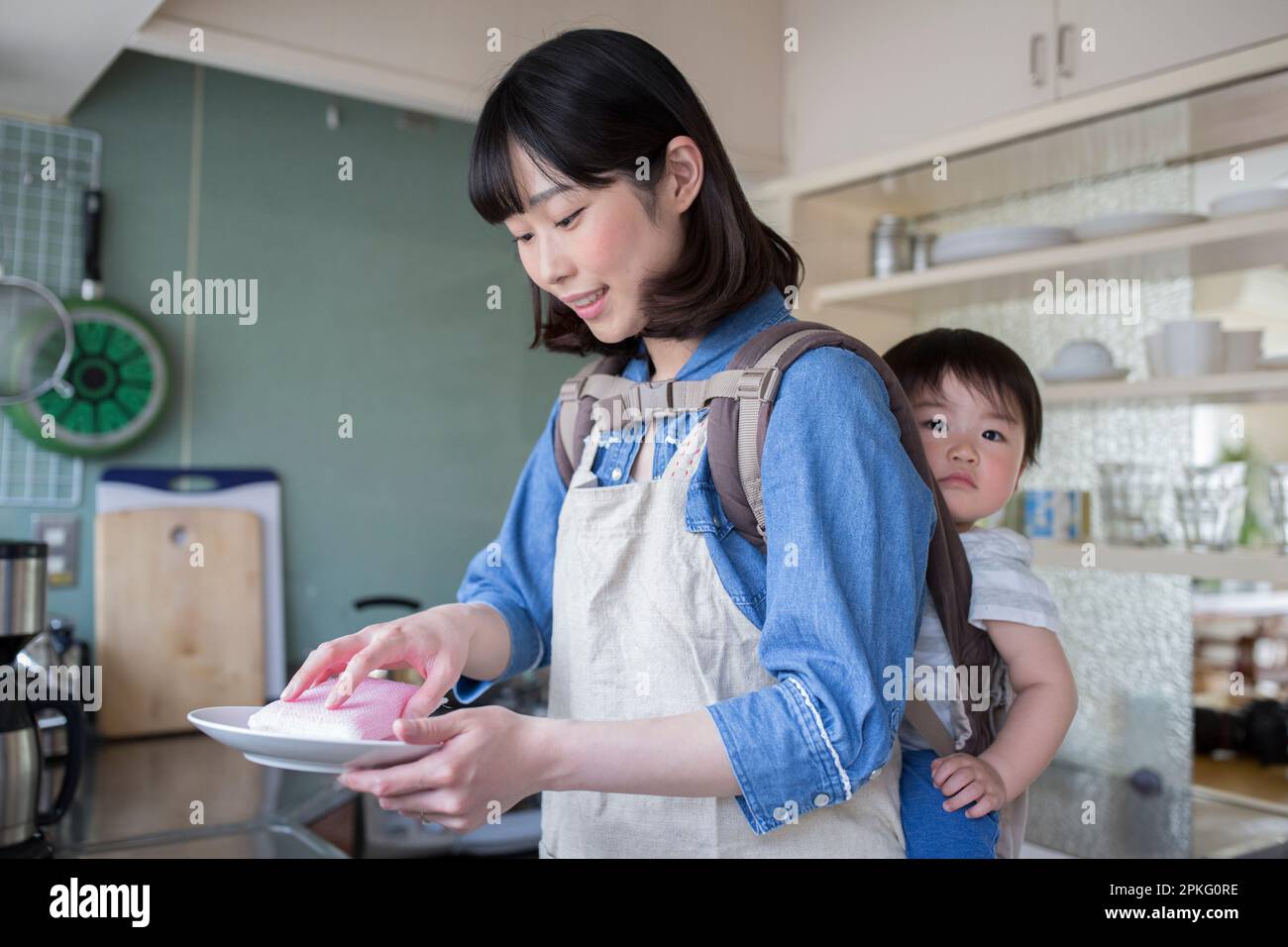 Mother washing dishes in the kitchen with child on back Stock Photo - Alamy