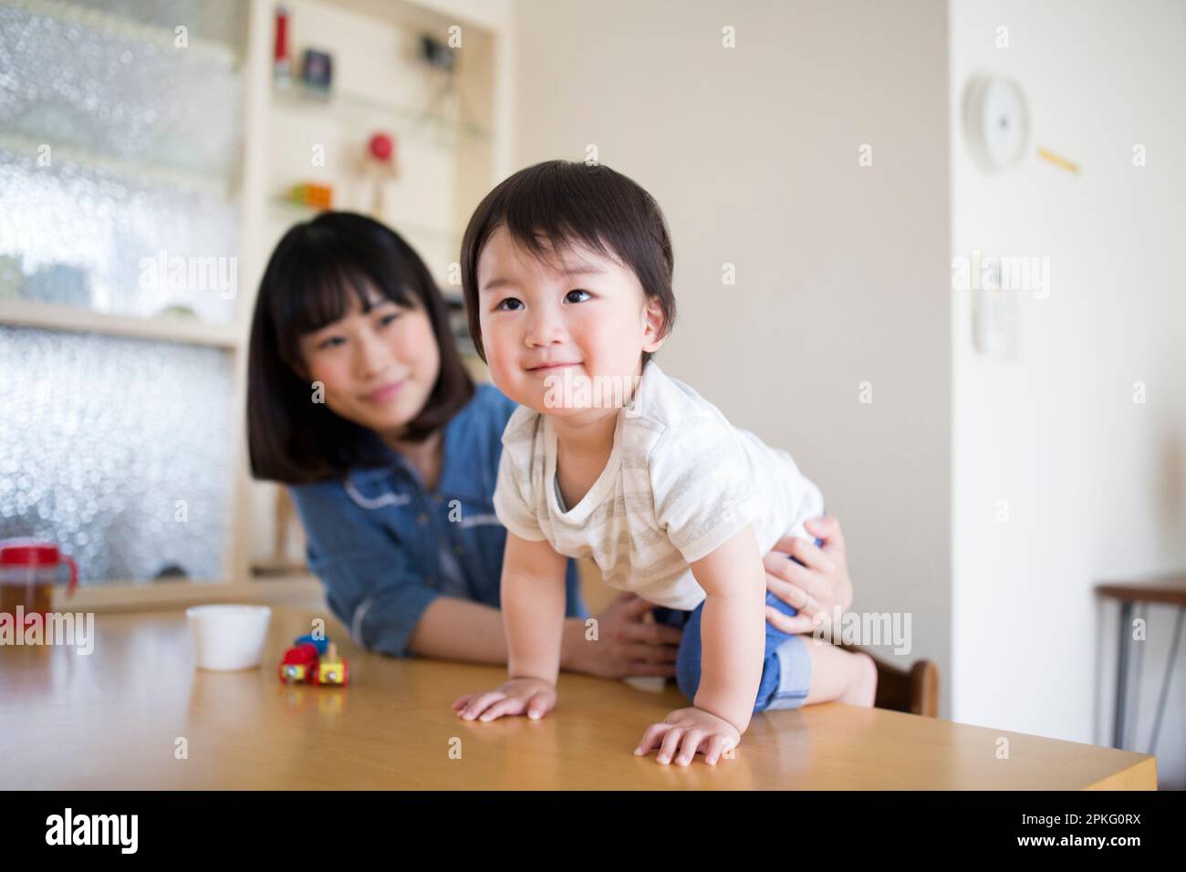 Toddler leaning over dining table with mother supporting him Stock ...