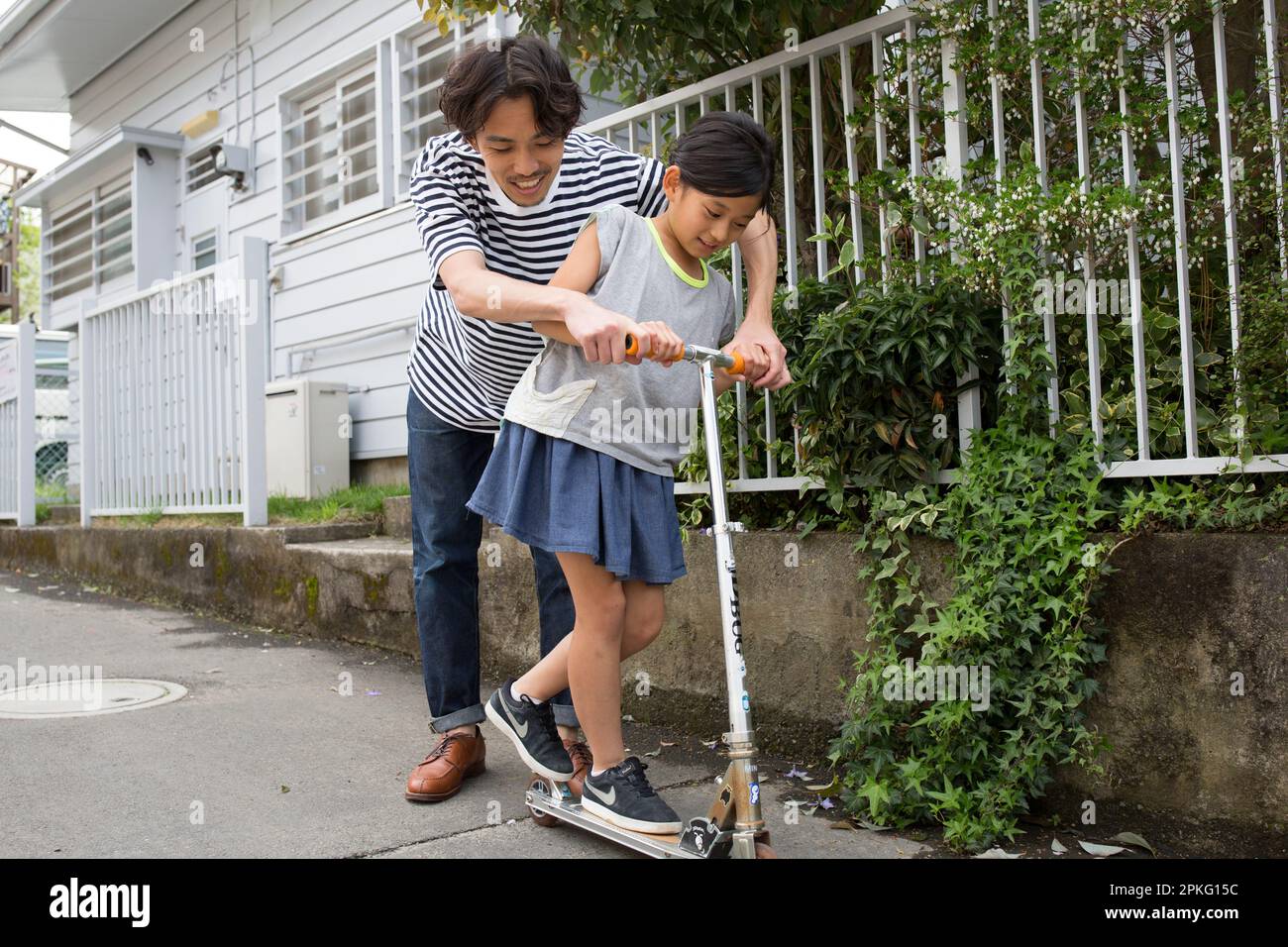 Father teaching his daughter how to ride a kickboard in front of his ...