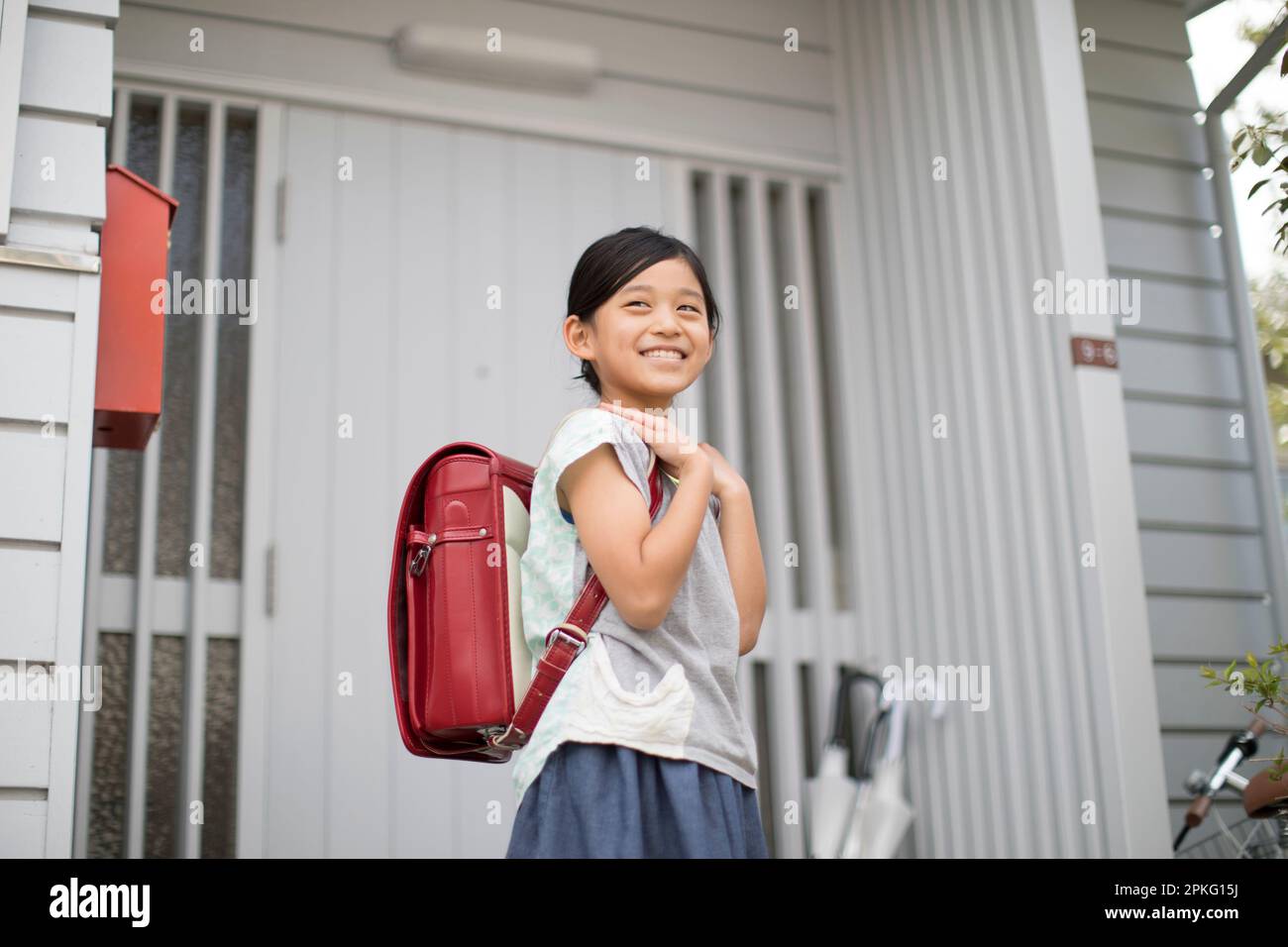 A girl with a school bag on her back smiling in front of her front door ...