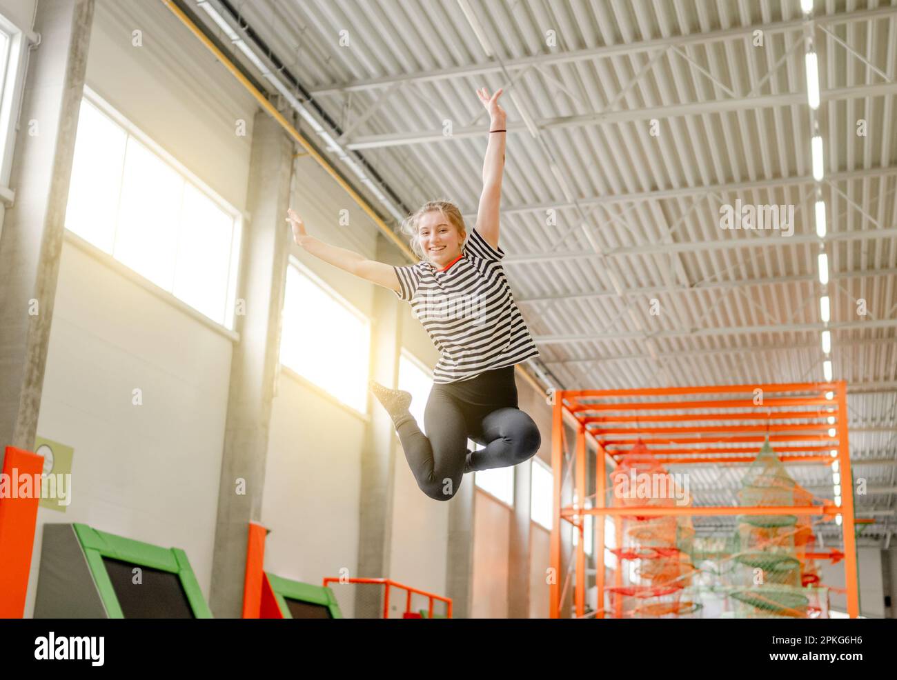Pretty girl in trampoline park jumping and making split pose in air ...