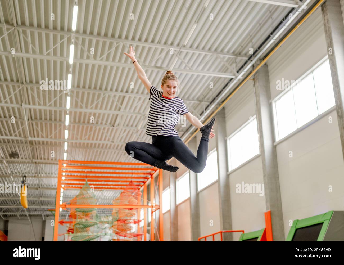 Pretty girl in trampoline park jumping and making split pose in air ...