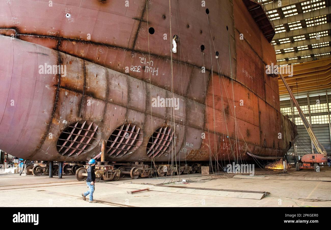 A worker walks by an unfinished 260-foot-long Eco Edison ship in ...