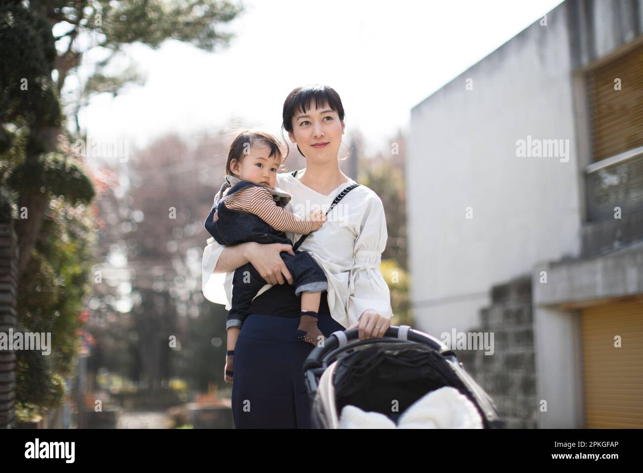 Mother pushing stroller while carrying baby Stock Photo - Alamy
