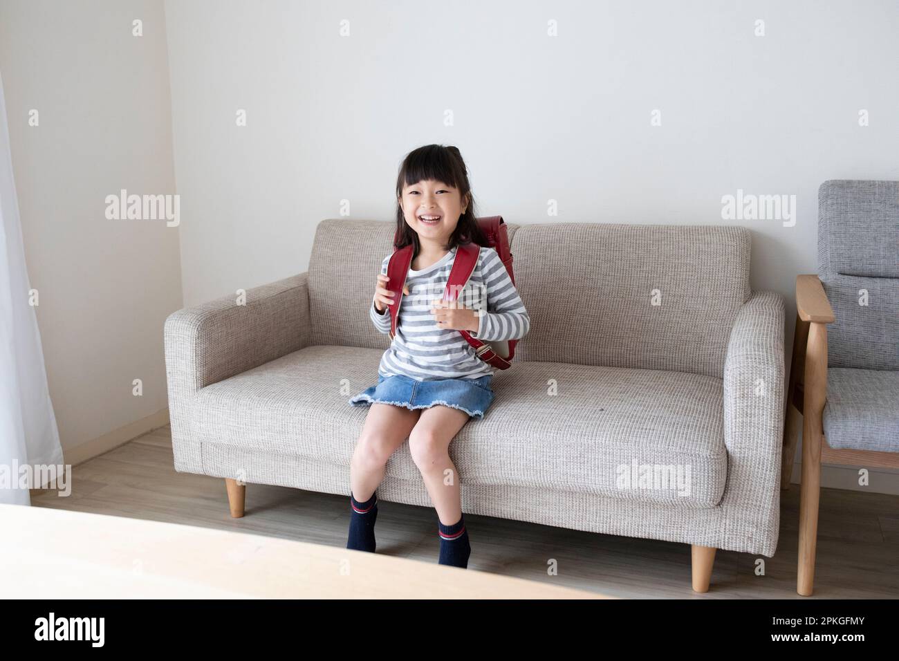 Girl sitting on couch with school bag on her back Stock Photo - Alamy