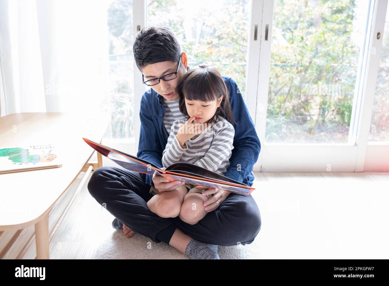 Girl sitting on father's lap and having a story book read to her Stock ...