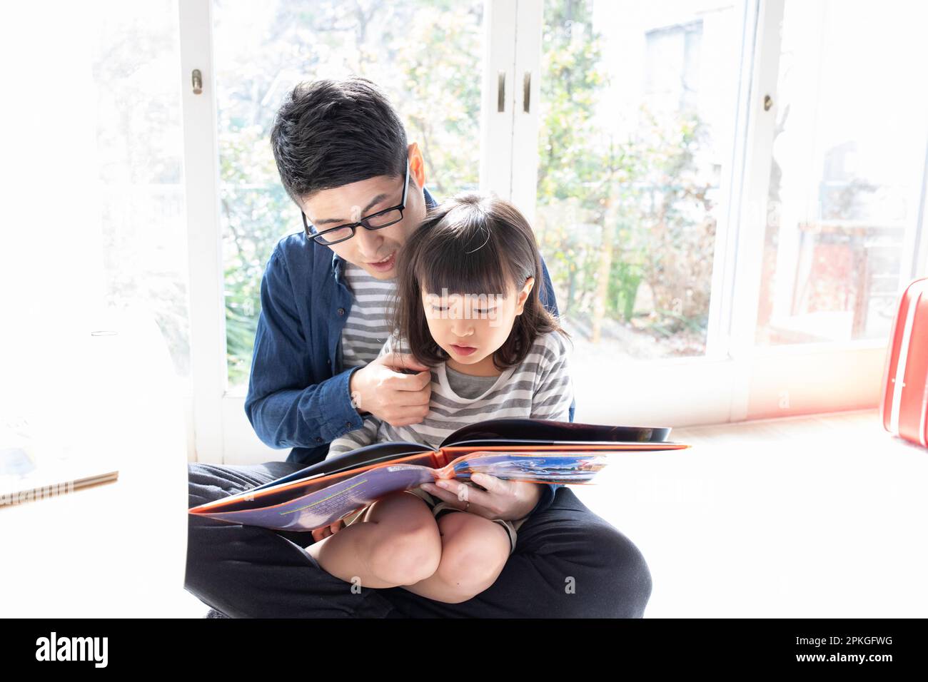 A girl sitting on her father's lap and having a picture book read to ...