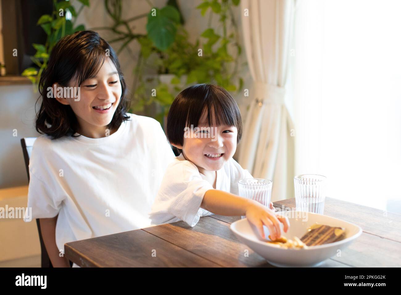 Little boy sitting on his sister's lap and smiling while eating a snack ...