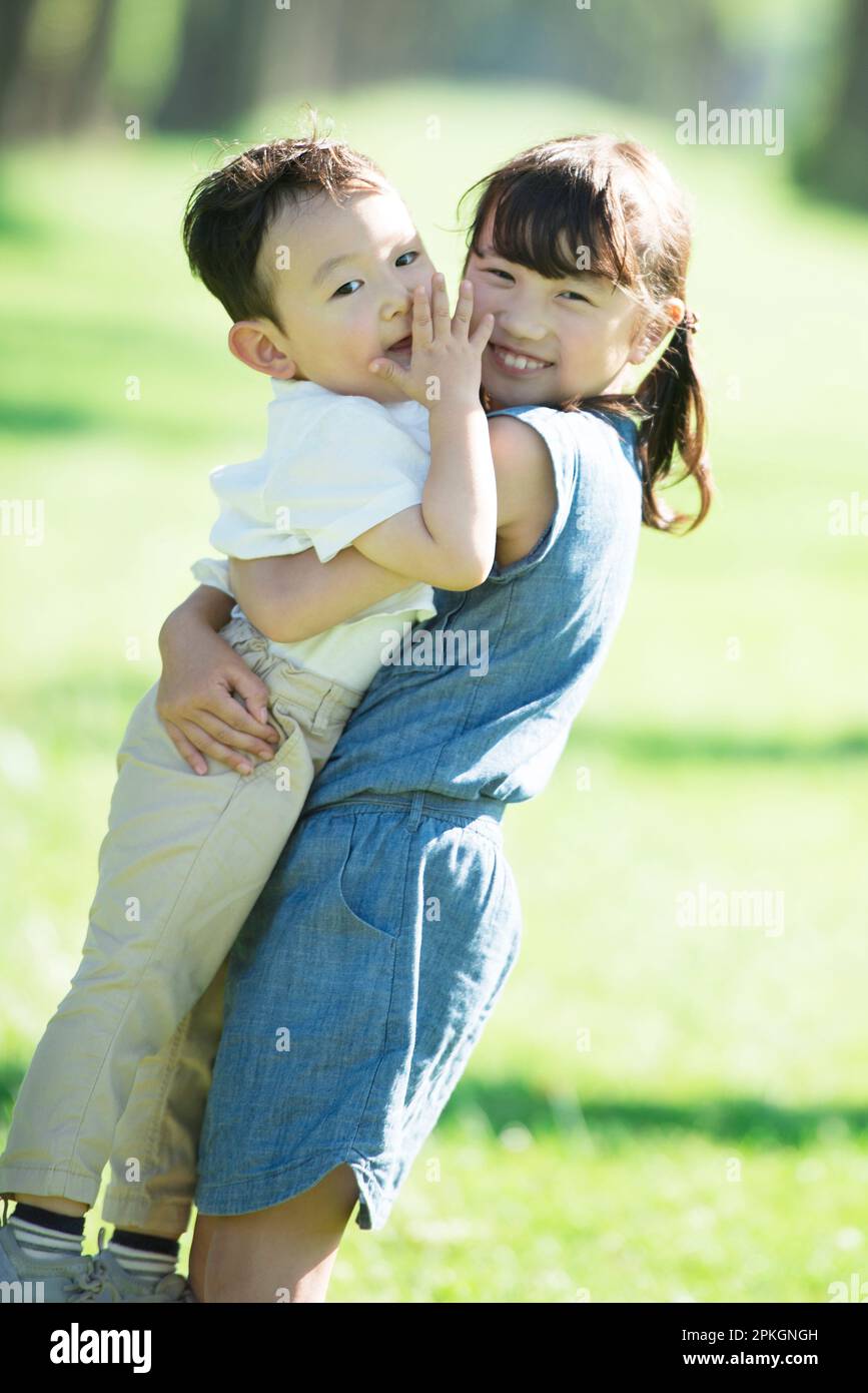 A sister and brother carrying a baby in their arms at a row of poplar ...