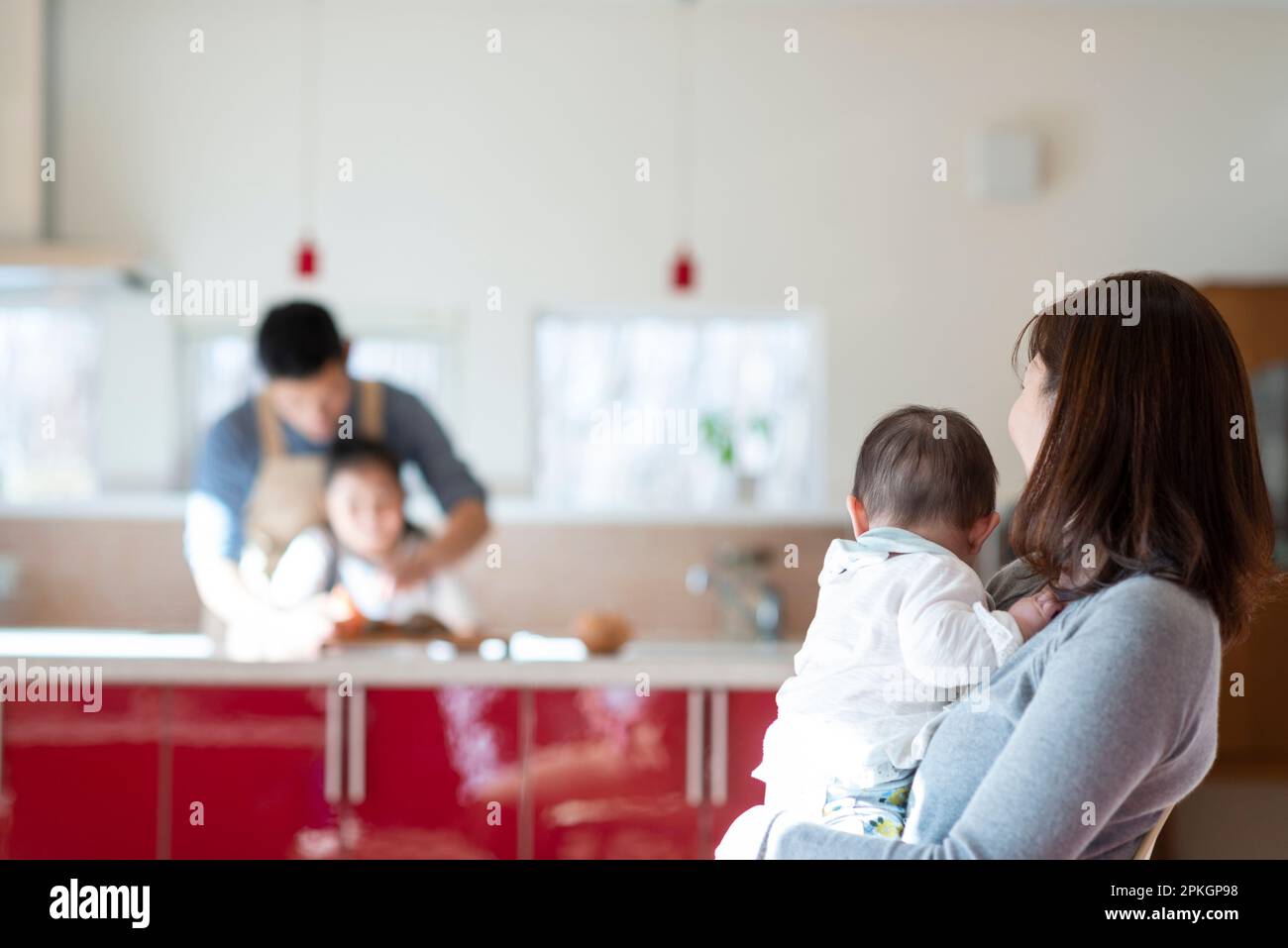 Mother watching family cooking in kitchen Stock Photo - Alamy