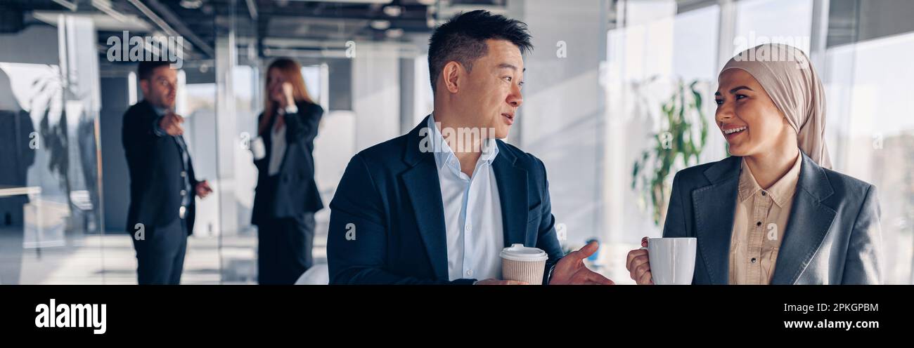 Two happy multiracial colleagues talking and drinking coffee during ...