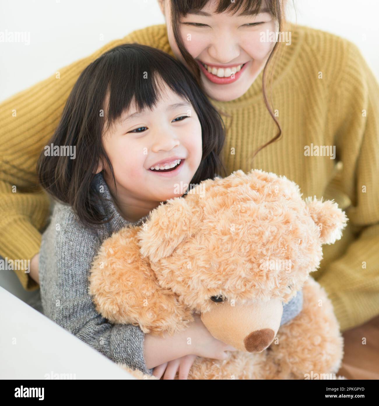 Mother cuddling with smiling girl holding stuffed bear Stock Photo - Alamy