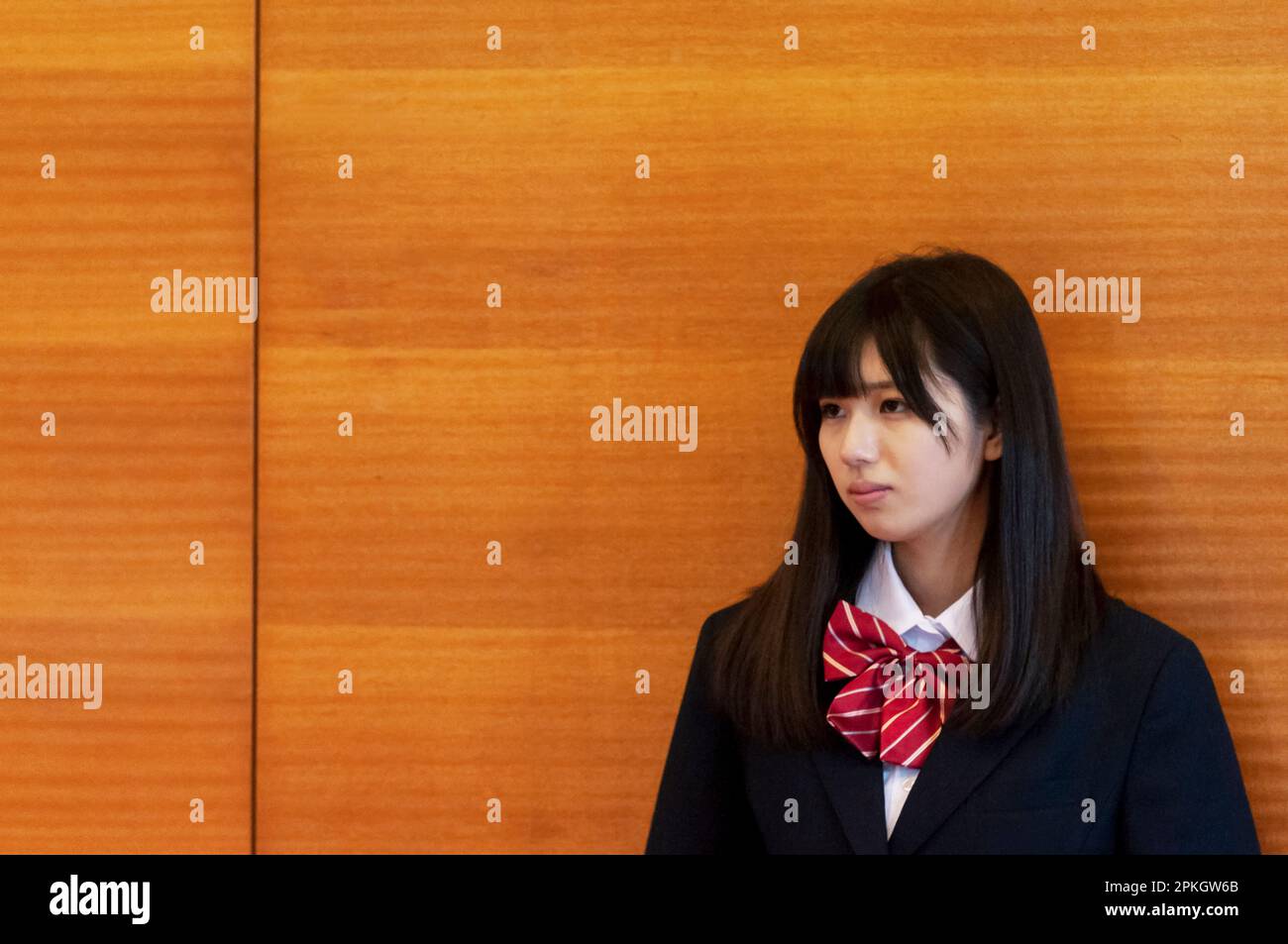 A female student leaning against a wall with a serious expression on ...