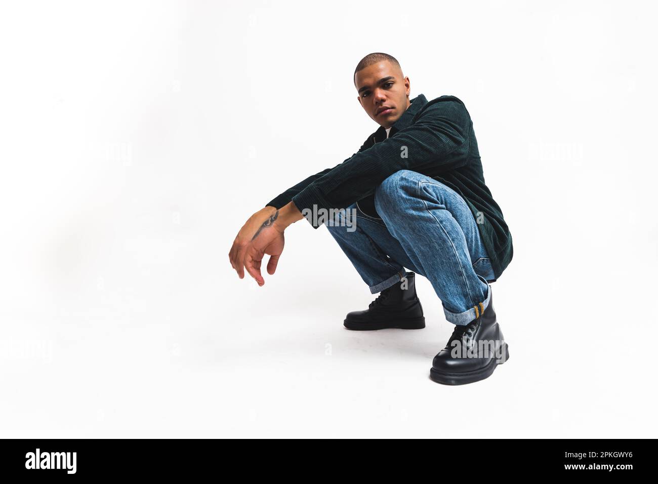Serious male fashion model posing in squat pose and looking to the ...