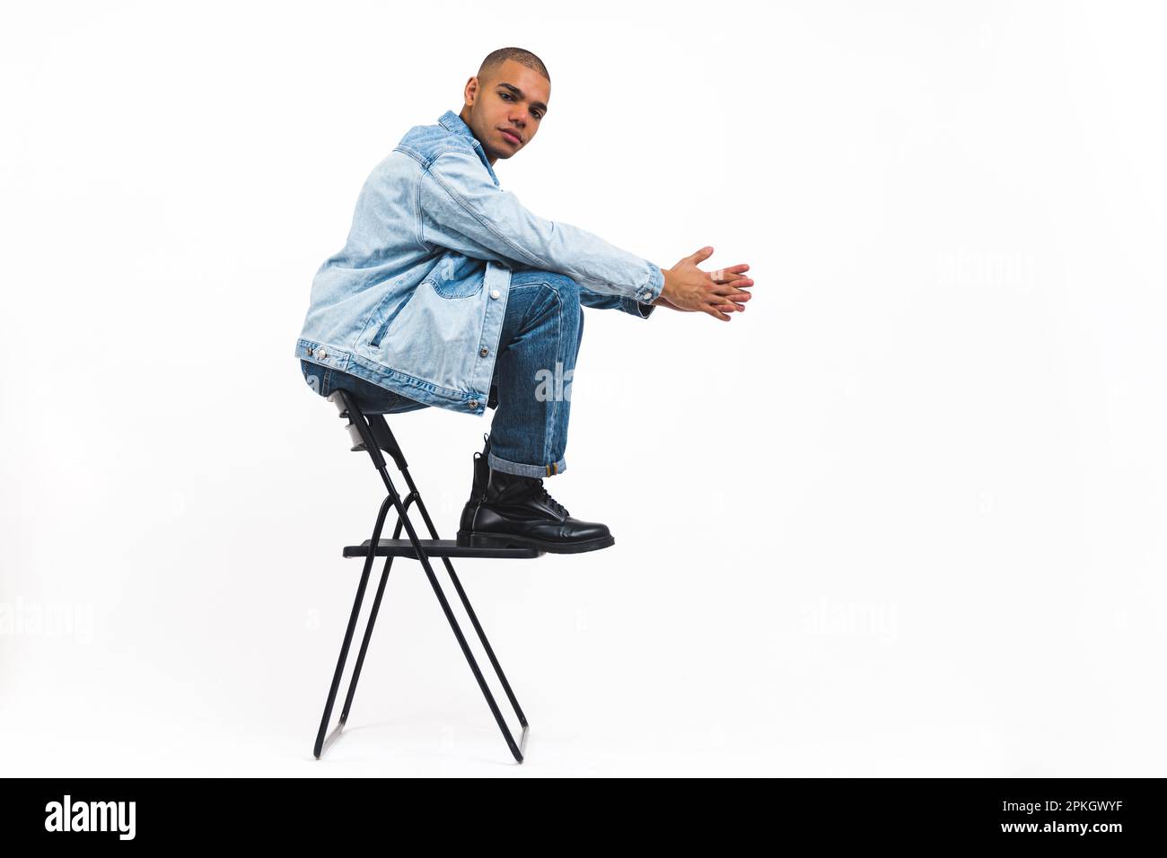 Young adult male model in denim set sitting on a chair in ...