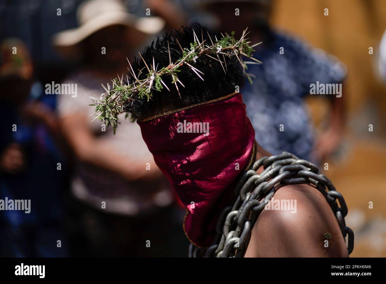 A masked penitent, wearing chains and a crown of thorns, takes part in ...