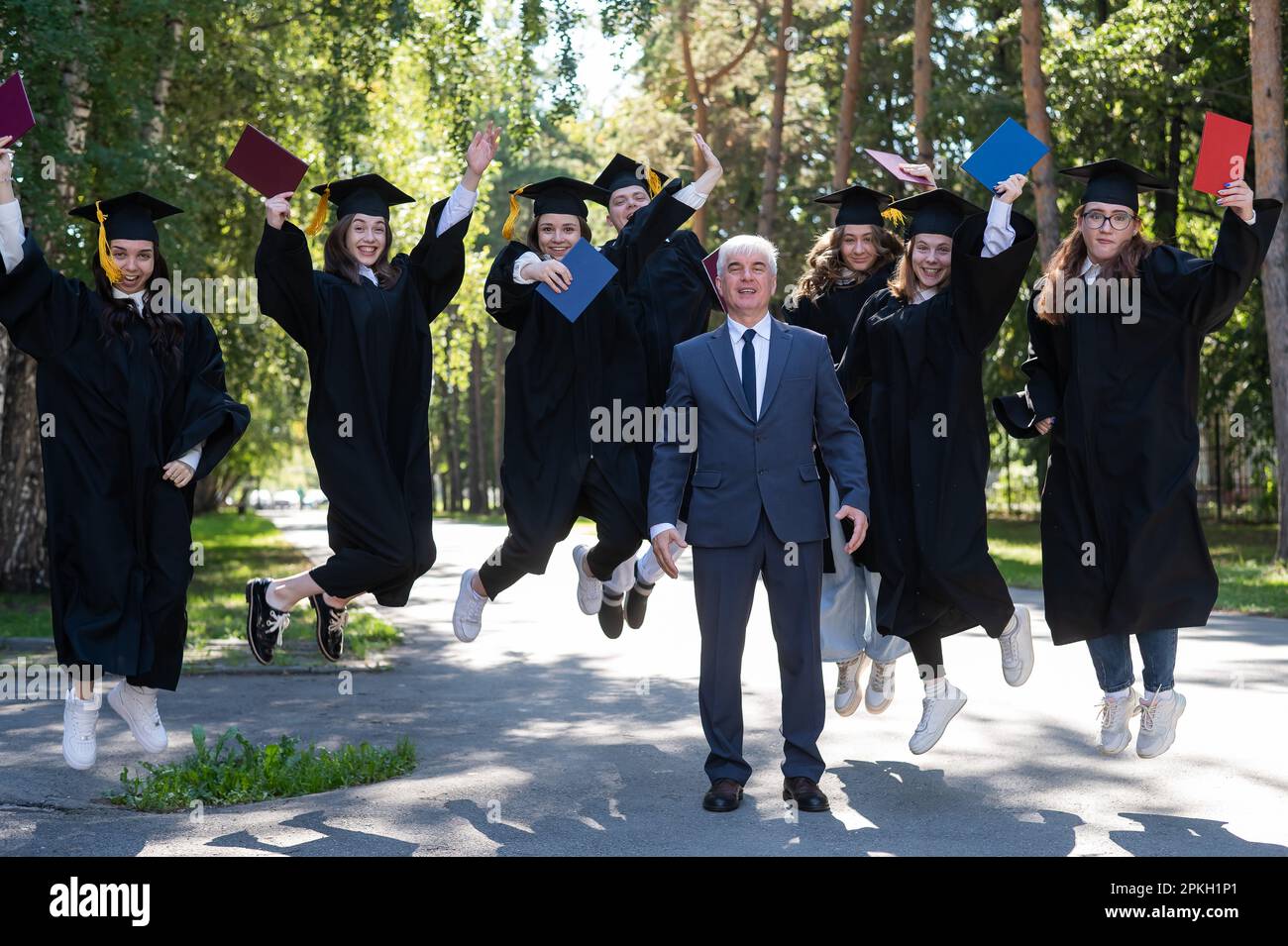 A university professor and seven robed graduates are jumping outdoors ...