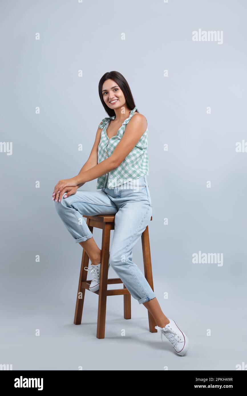 Beautiful young woman sitting on stool against light grey background ...